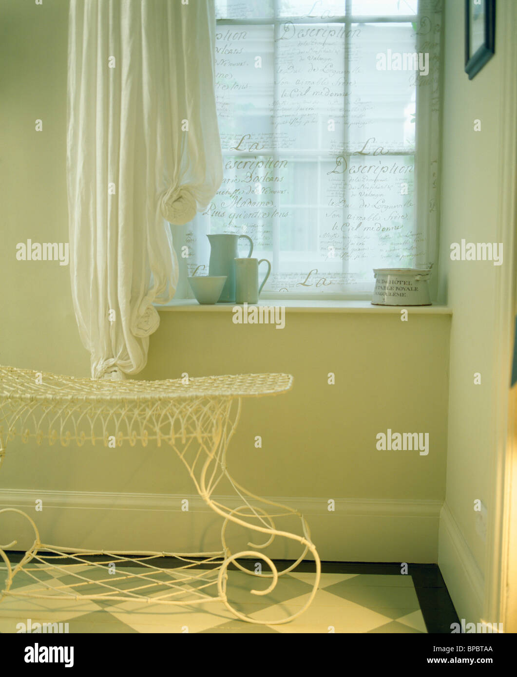 Ornate white metal table below window with white voile curtain in ...