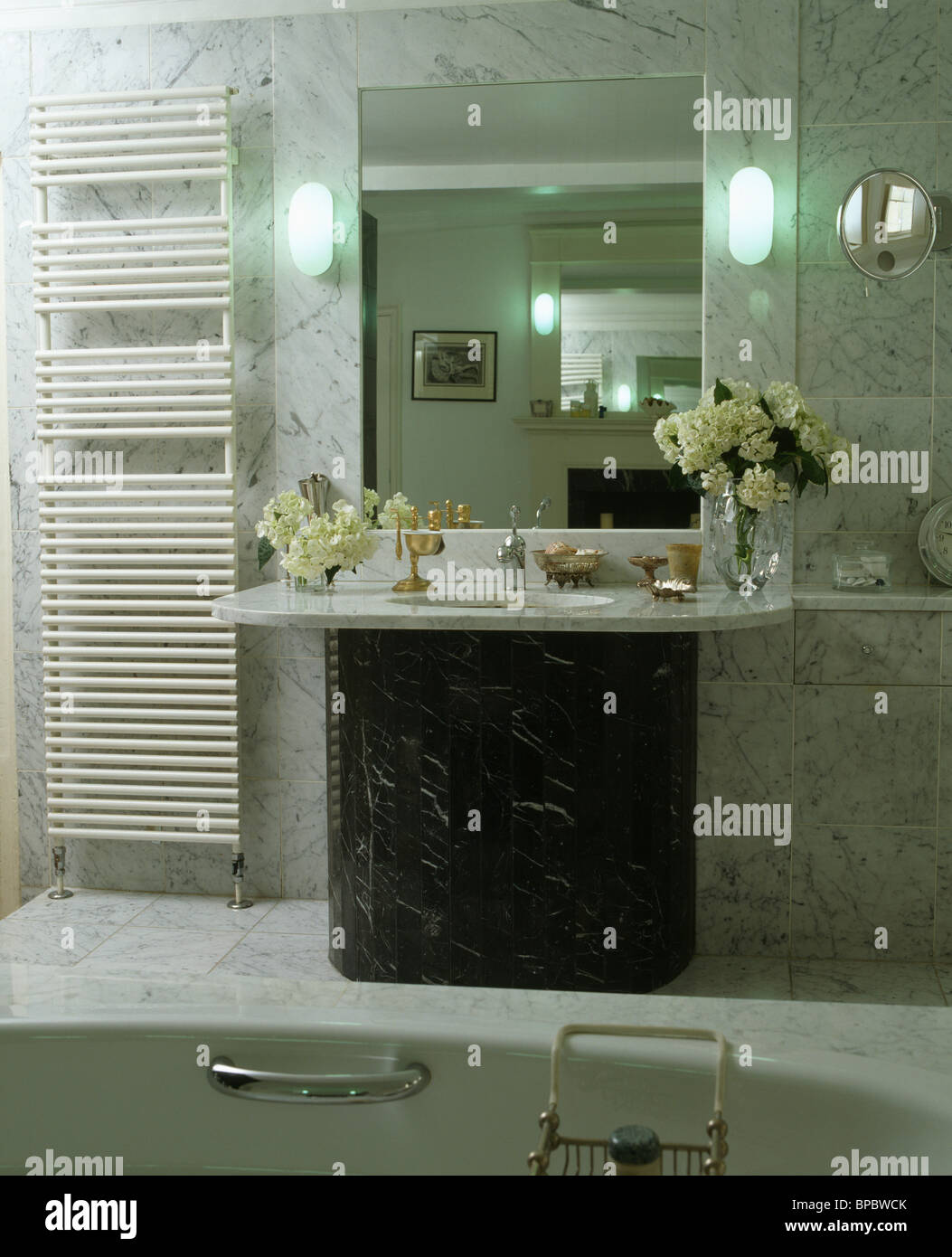 Vertical white radiator on wall beside mirror above vanity unit in ...