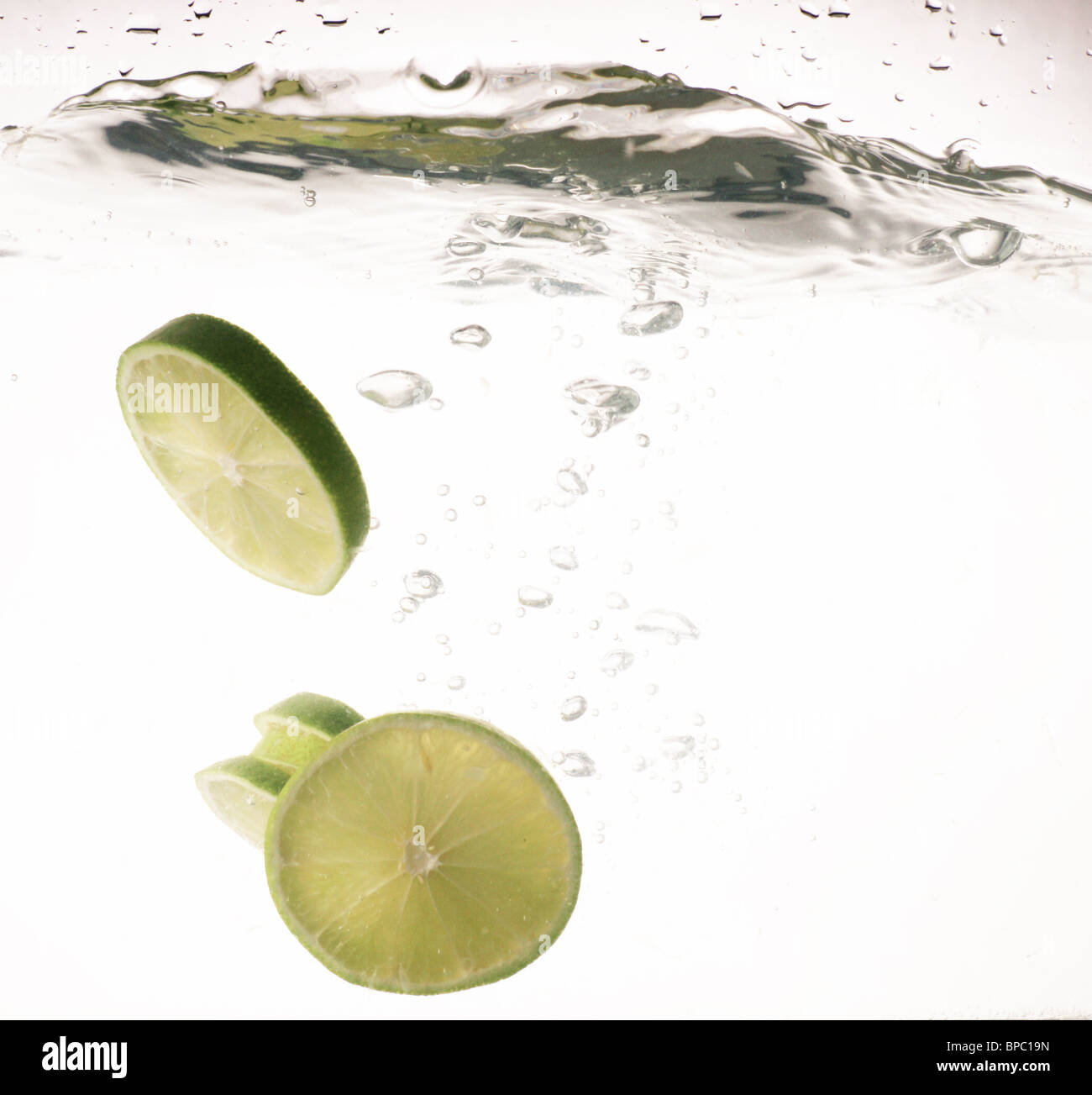 Lime slices drop into a water with a splash Stock Photo - Alamy