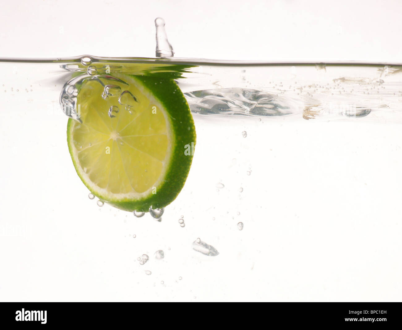 Lime slices drop into a water with a splash Stock Photo - Alamy