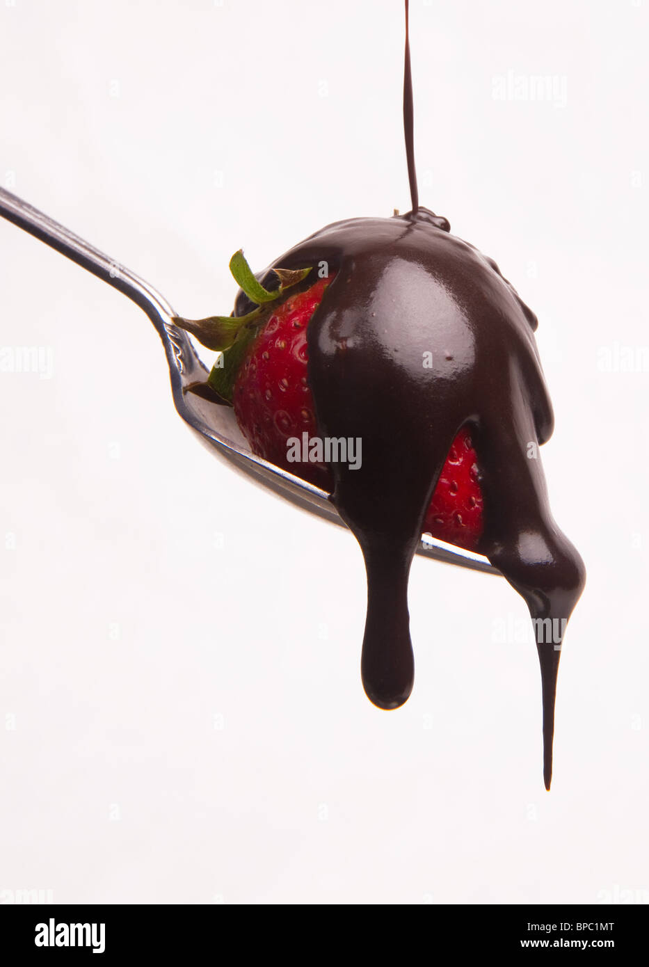 Chocolate Syrup drops onto a Strawberry sitting on a Spoon isolated on ...