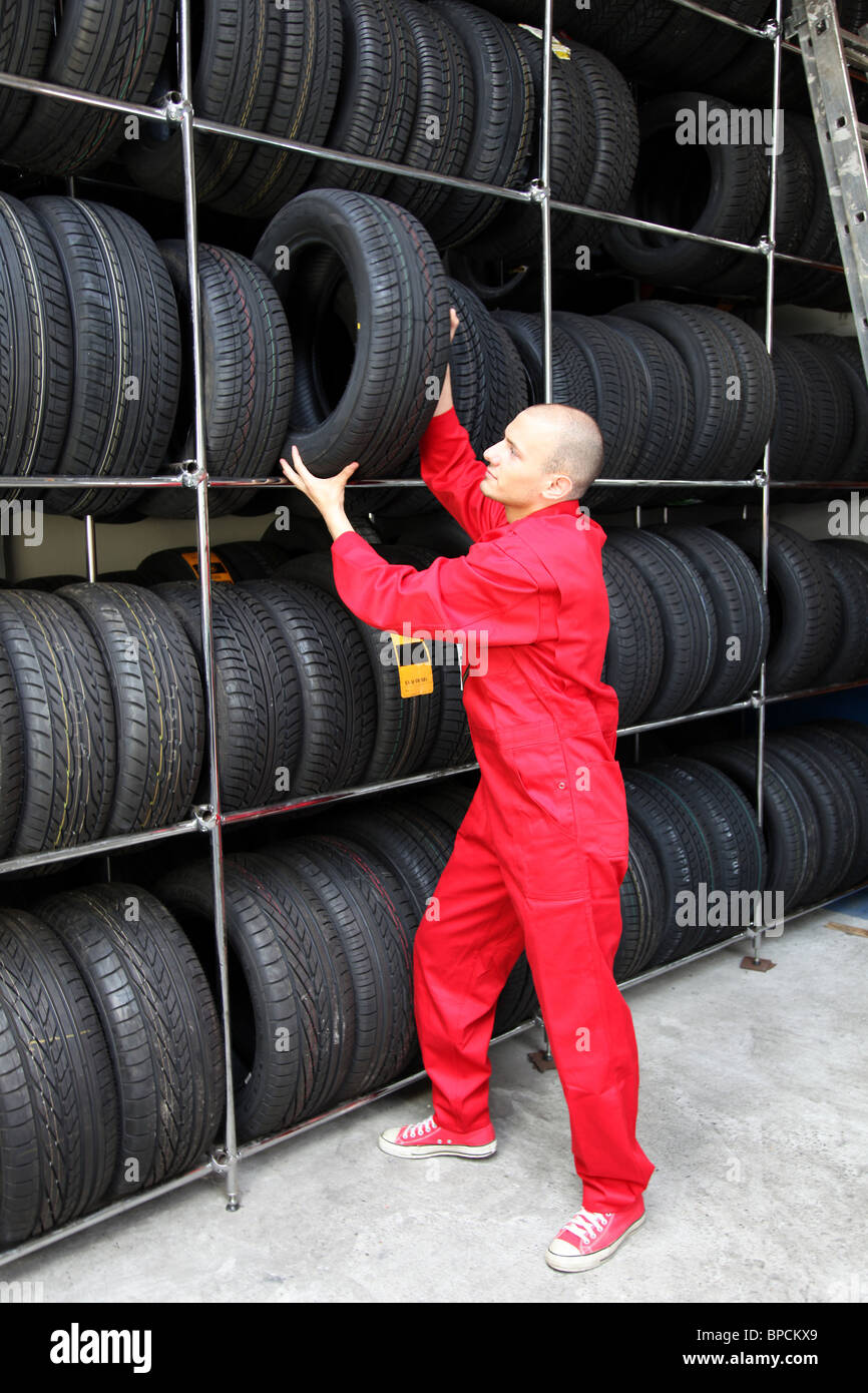 A working mechanic in a garage standing next to a rack full of tires ...