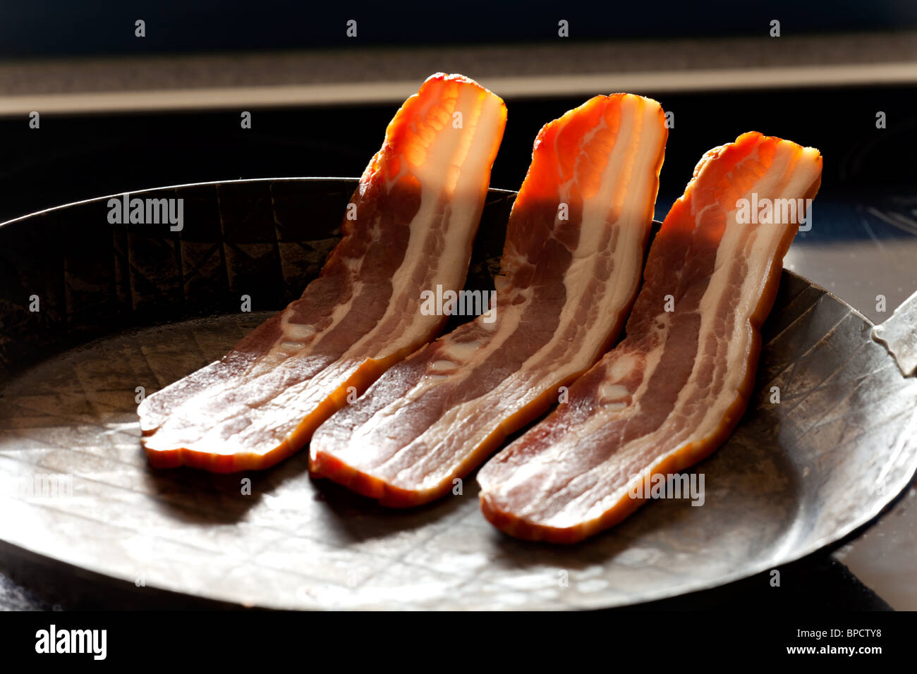 three stripes of bacon in a pan Stock Photo - Alamy