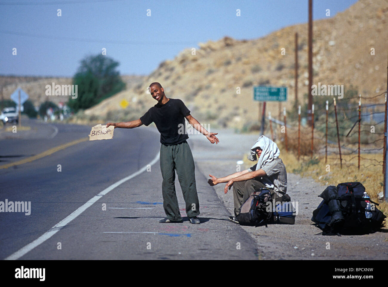 Two backpackers hitch hiking on the side of the road in the sun Stock ...