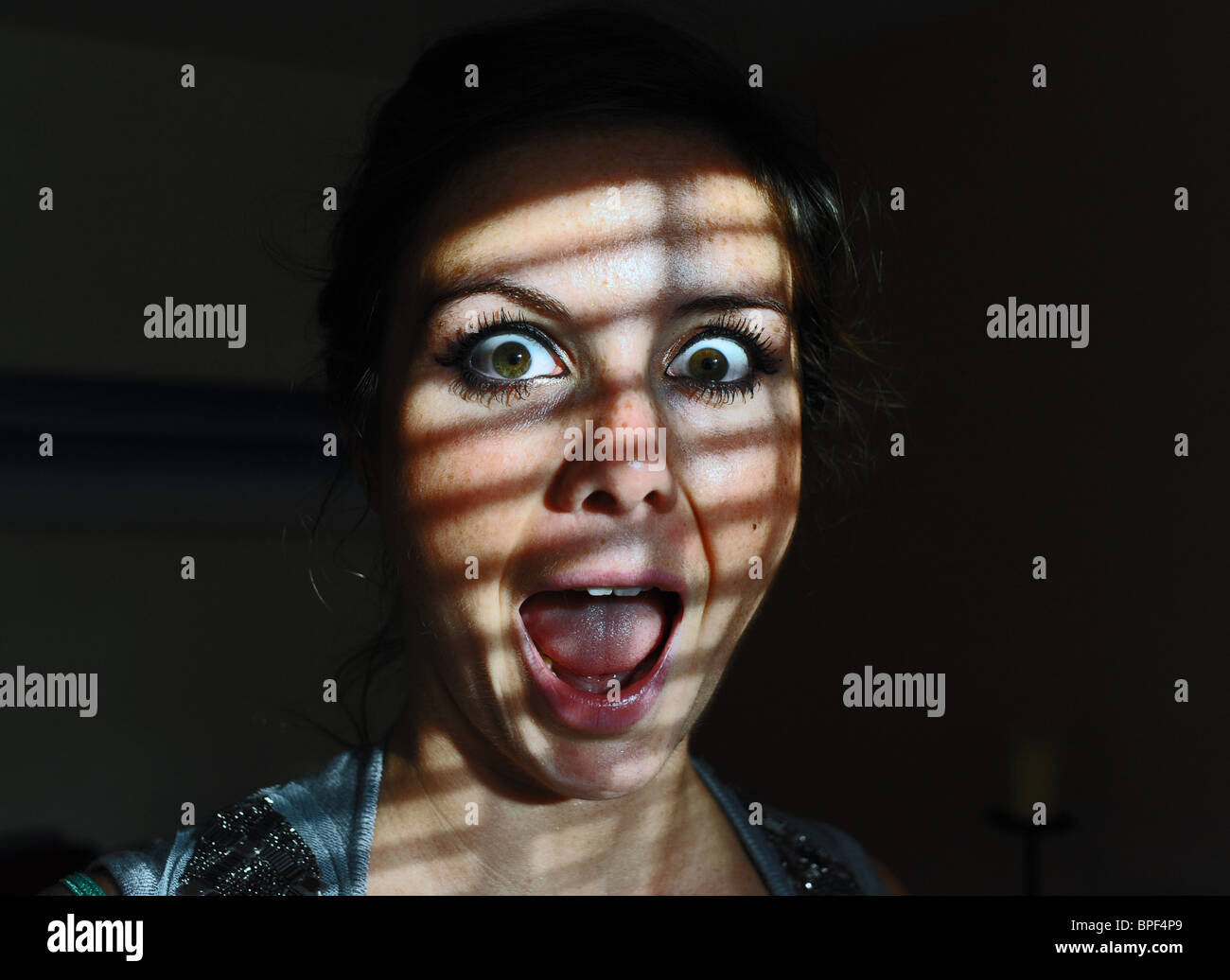Young attractive woman with light shadows across face making startled ...
