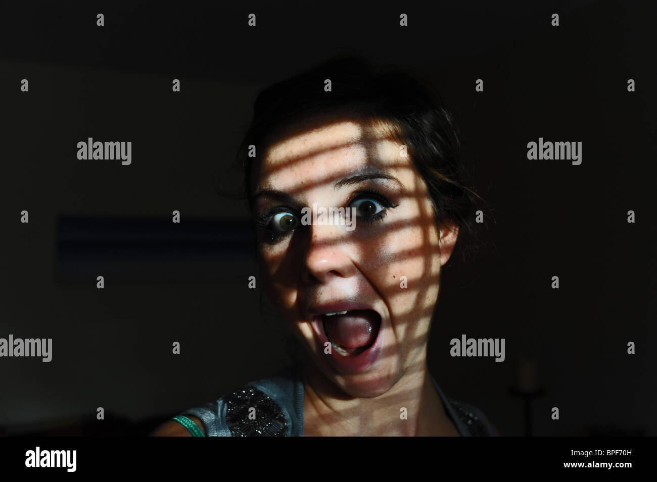 Young attractive woman with light shadows across face making startled ...