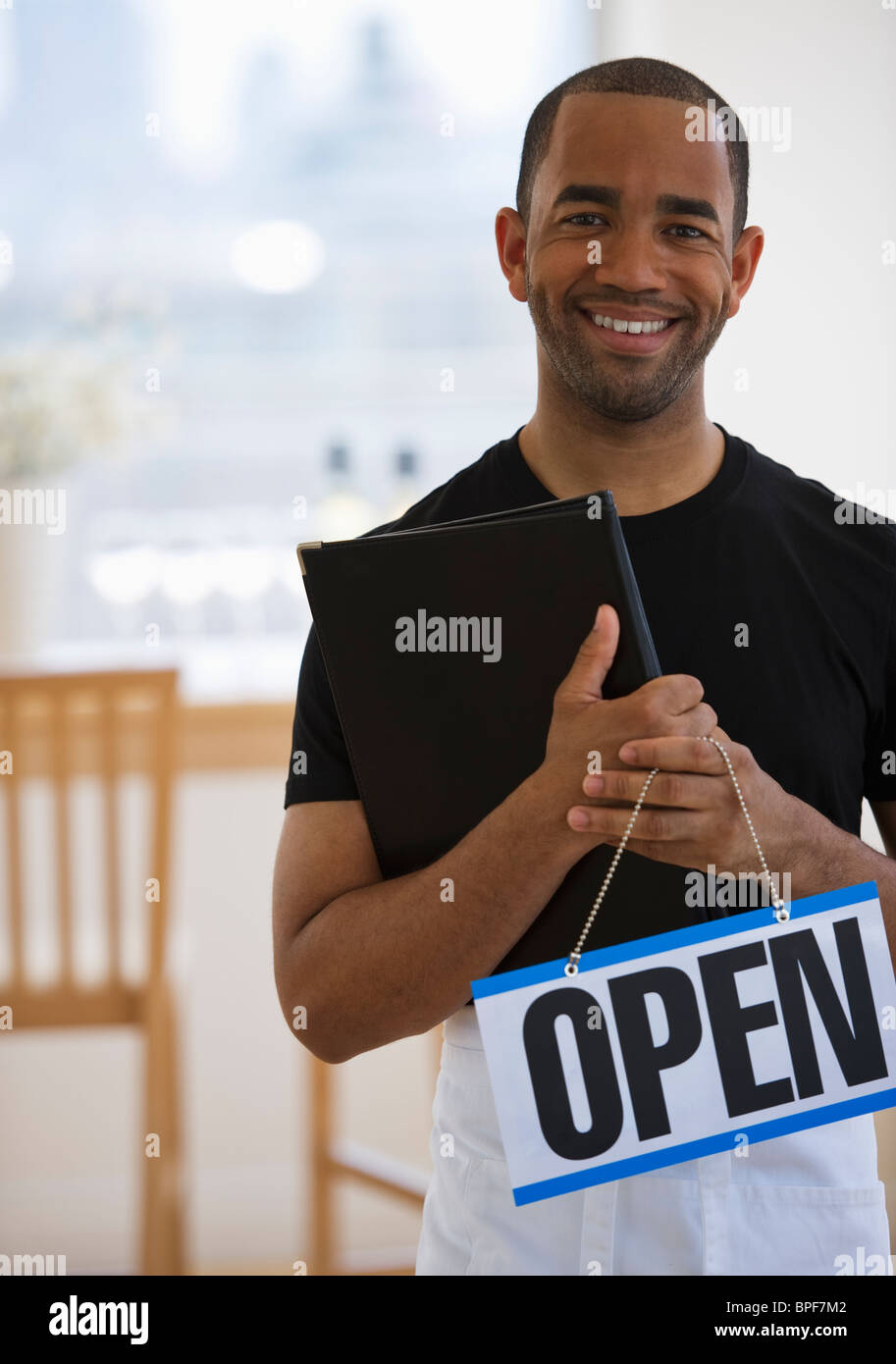 Mixed race waiter in restaurant holding menu and open sign Stock Photo ...