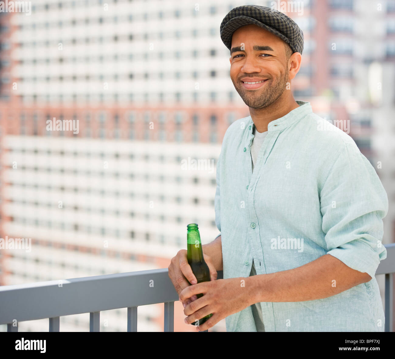 Mixed race man drinking beer near railing Stock Photo - Alamy