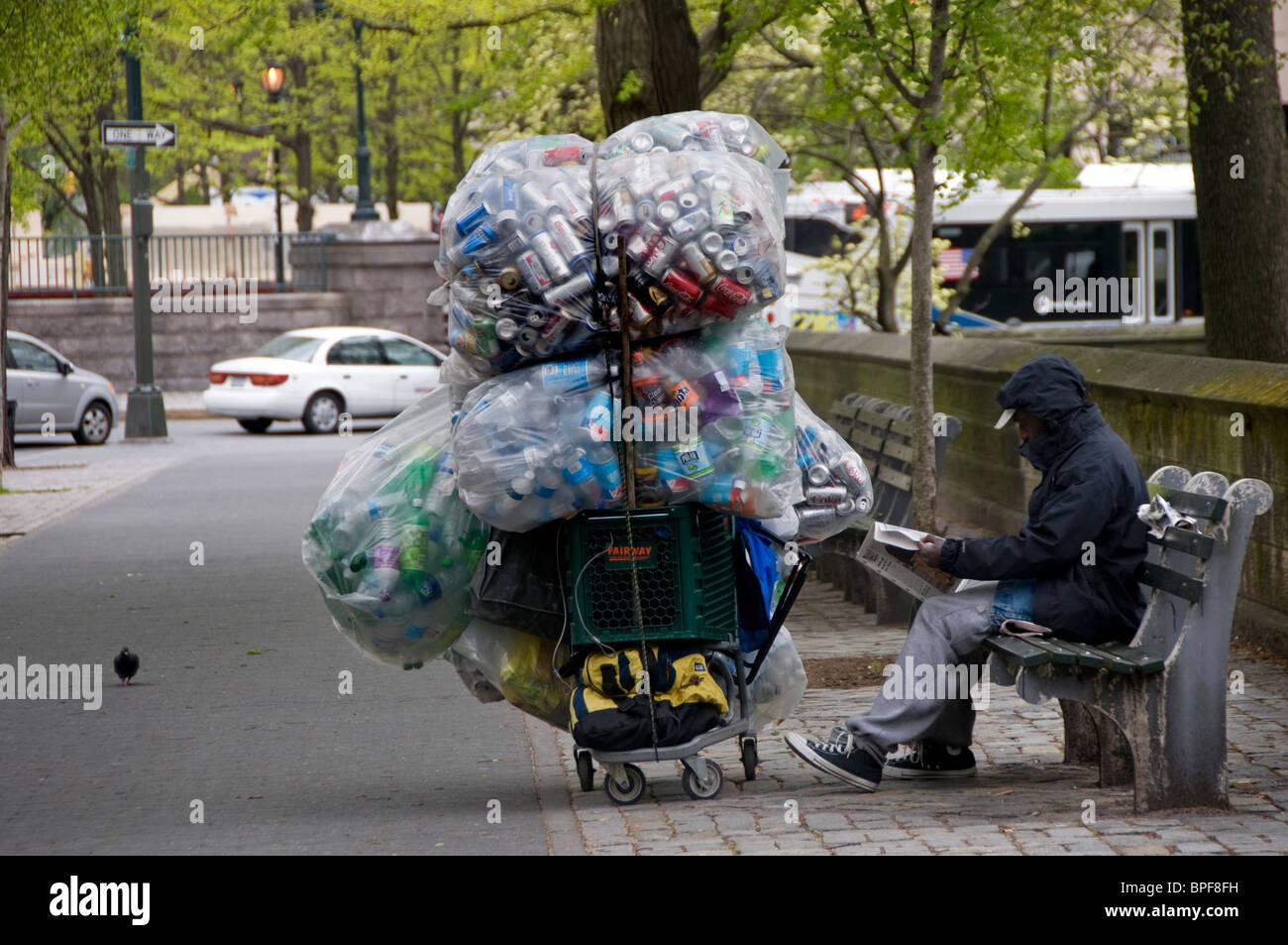 Homeless man sitting on park bench with trolley of recycled tin cans ...
