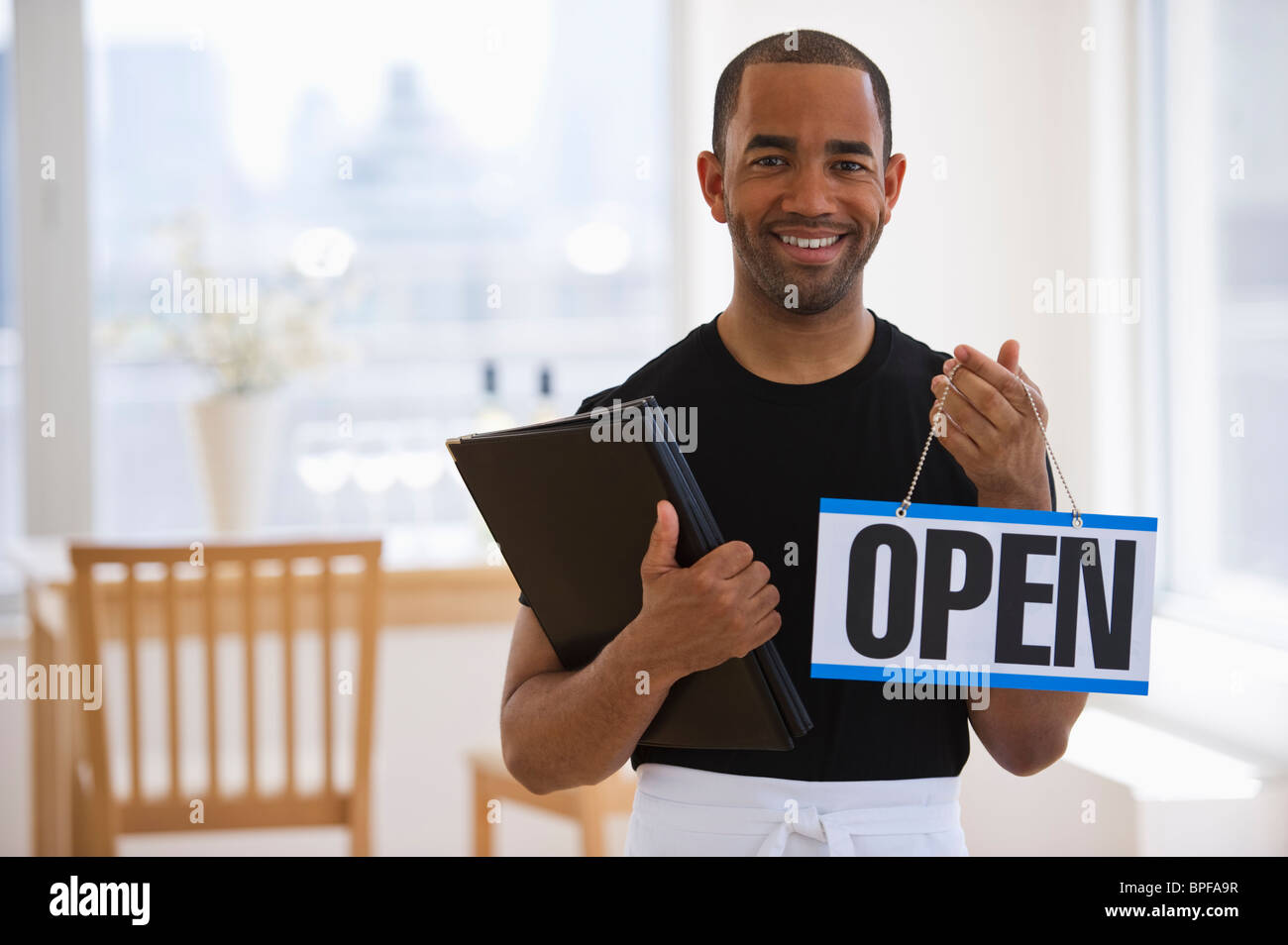 Mixed race waiter in restaurant holding menu and open sign Stock Photo ...