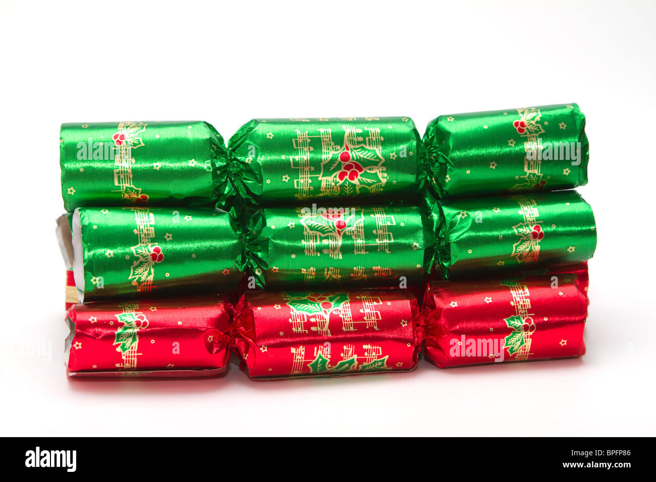 A stack of green and red foil Christmas crackers on a white background ...