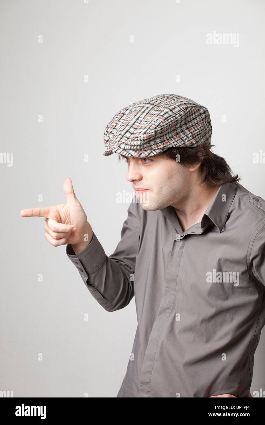 Young man wearing a flat cap and gray shirt pointing with his fingers ...