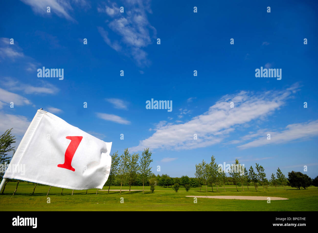 Closeup of golf flag on golf course. The sky is blue with white clouds ...