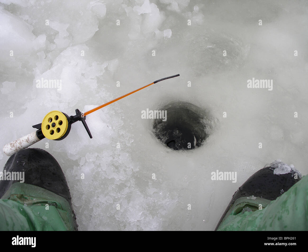 Two legs and the fishing rod. Hole in the ice Stock Photo - Alamy