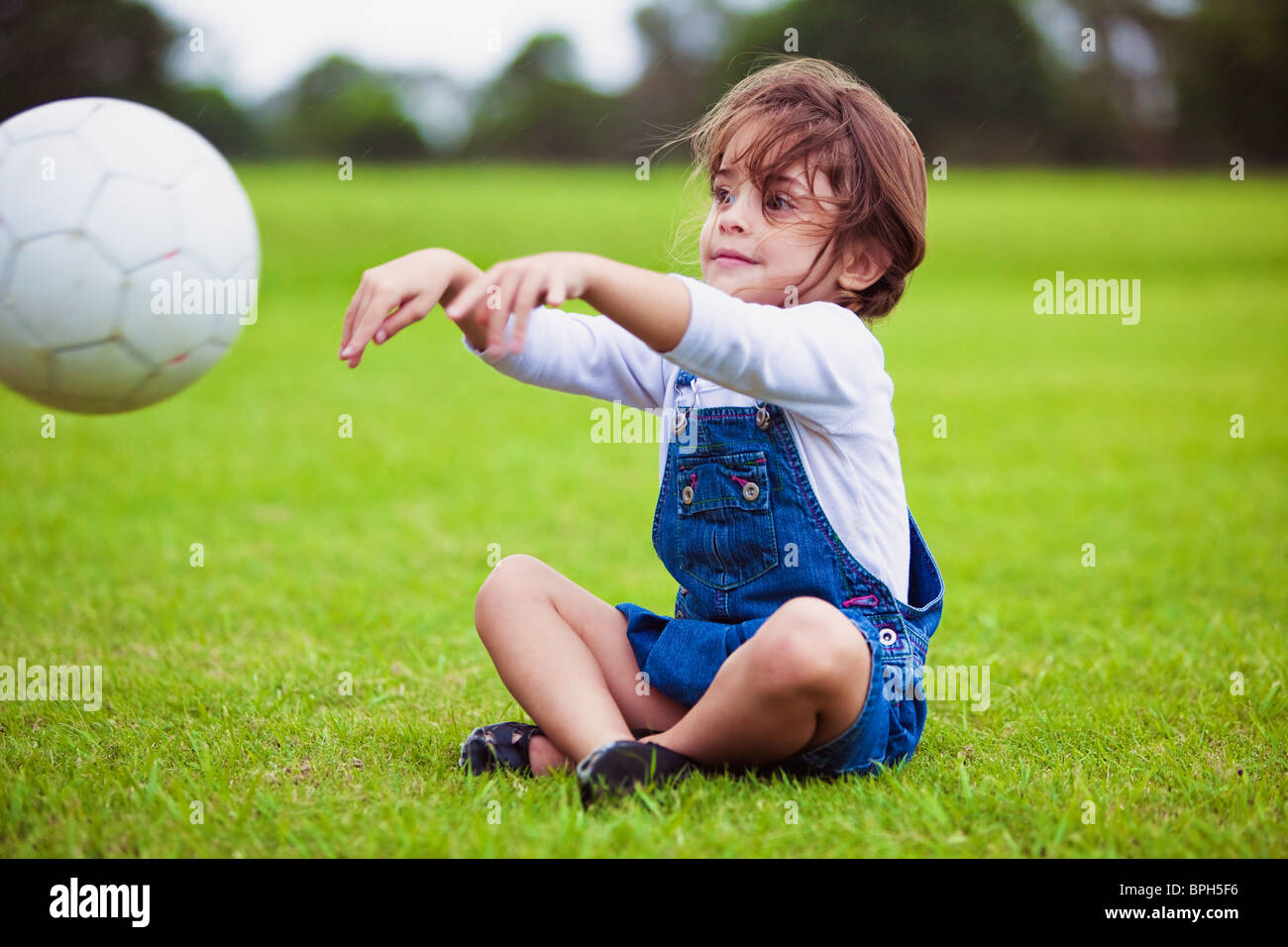 Young girl sitting on a grass throwing large ball Stock Photo - Alamy
