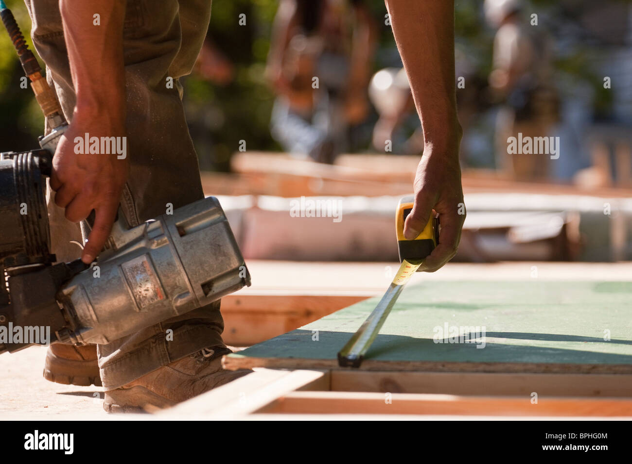Carpenters holding a nail gun and measuring a board Stock Photo - Alamy