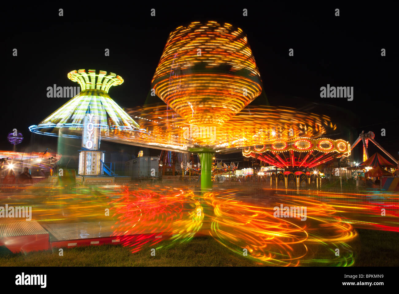 Colorfully illuminated rides, with the Sizzler in the foreground, spin ...