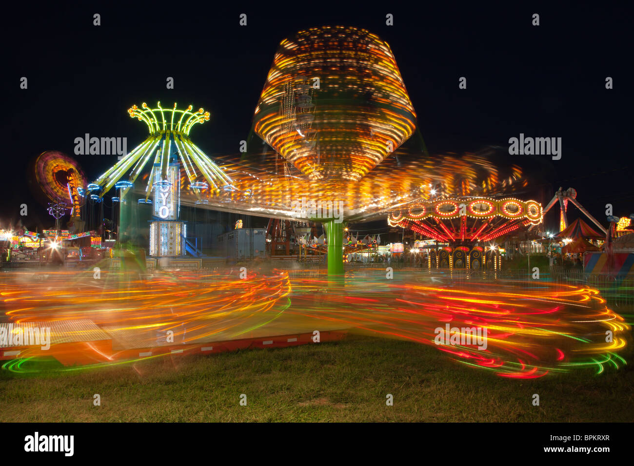 Colorfully illuminated rides, with the Sizzler in the foreground, spin ...
