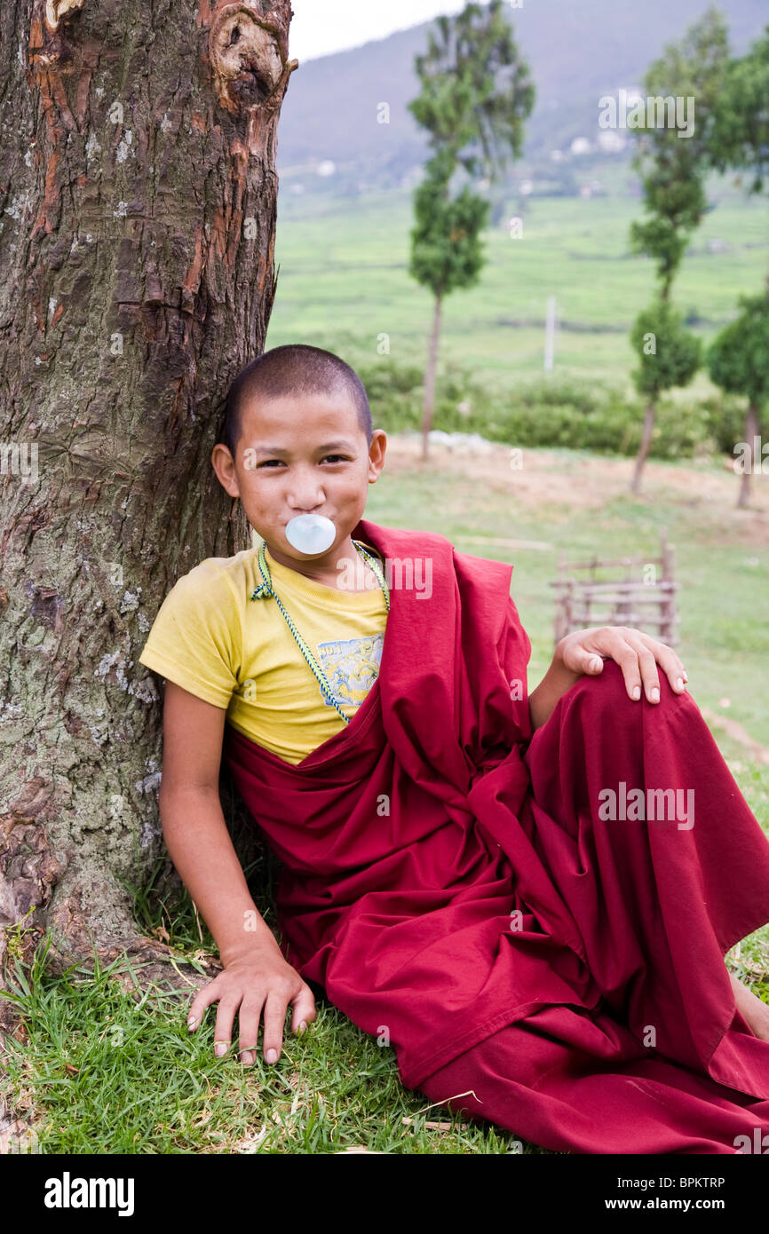 Young Buddhist monk blows a bubble with bubble gum as he sits under a ...