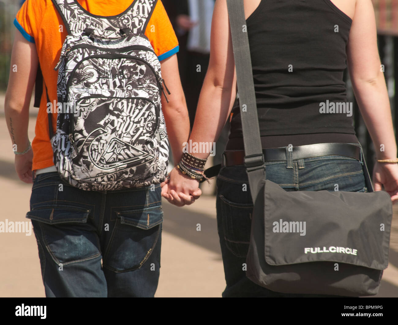 A young couple wearing backpacks walk hand in hand through Glasgow city ...