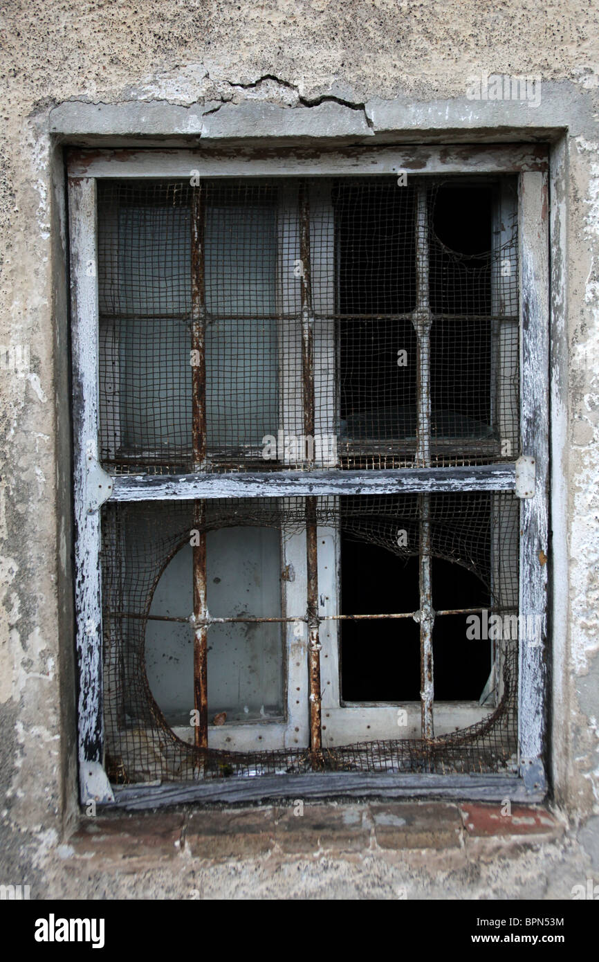Old barred window with flaking paint and a mesh cover of broken metal ...