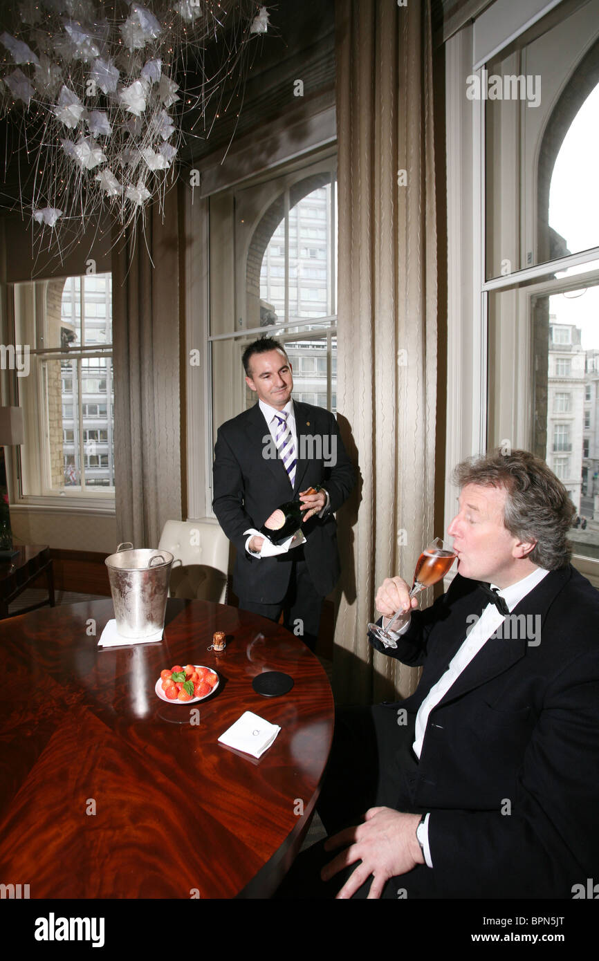 Man dressed in black tie drinking champagne served by personal butler ...