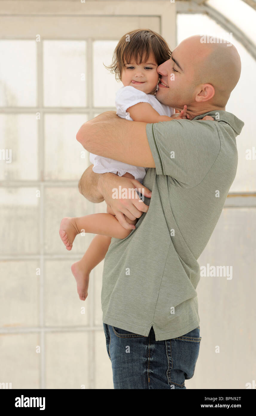 Young father embracing baby girl in front of window in bright home ...