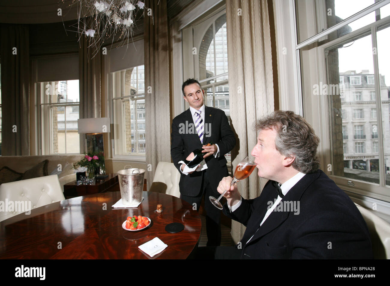 A man dressed in black tie drinking champagne served by personal butler ...