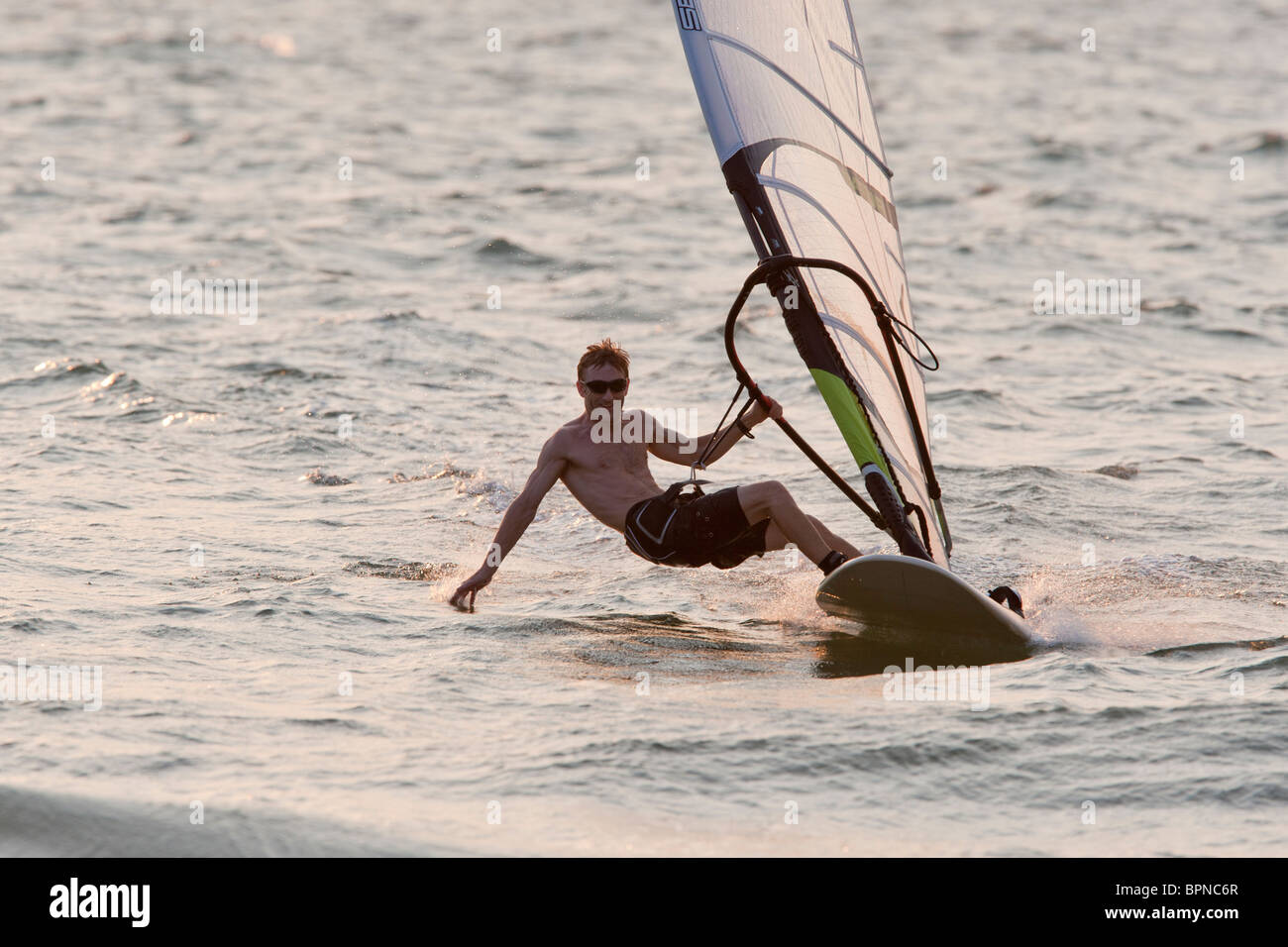A windsurfer runs his hands through the water Stock Photo - Alamy