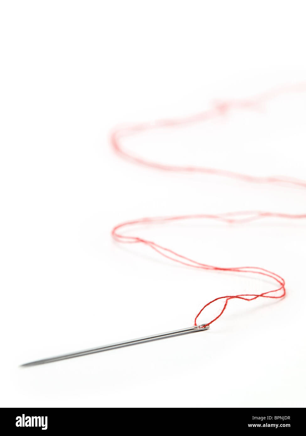 sewing needle with red thread over white background, focus on the ...