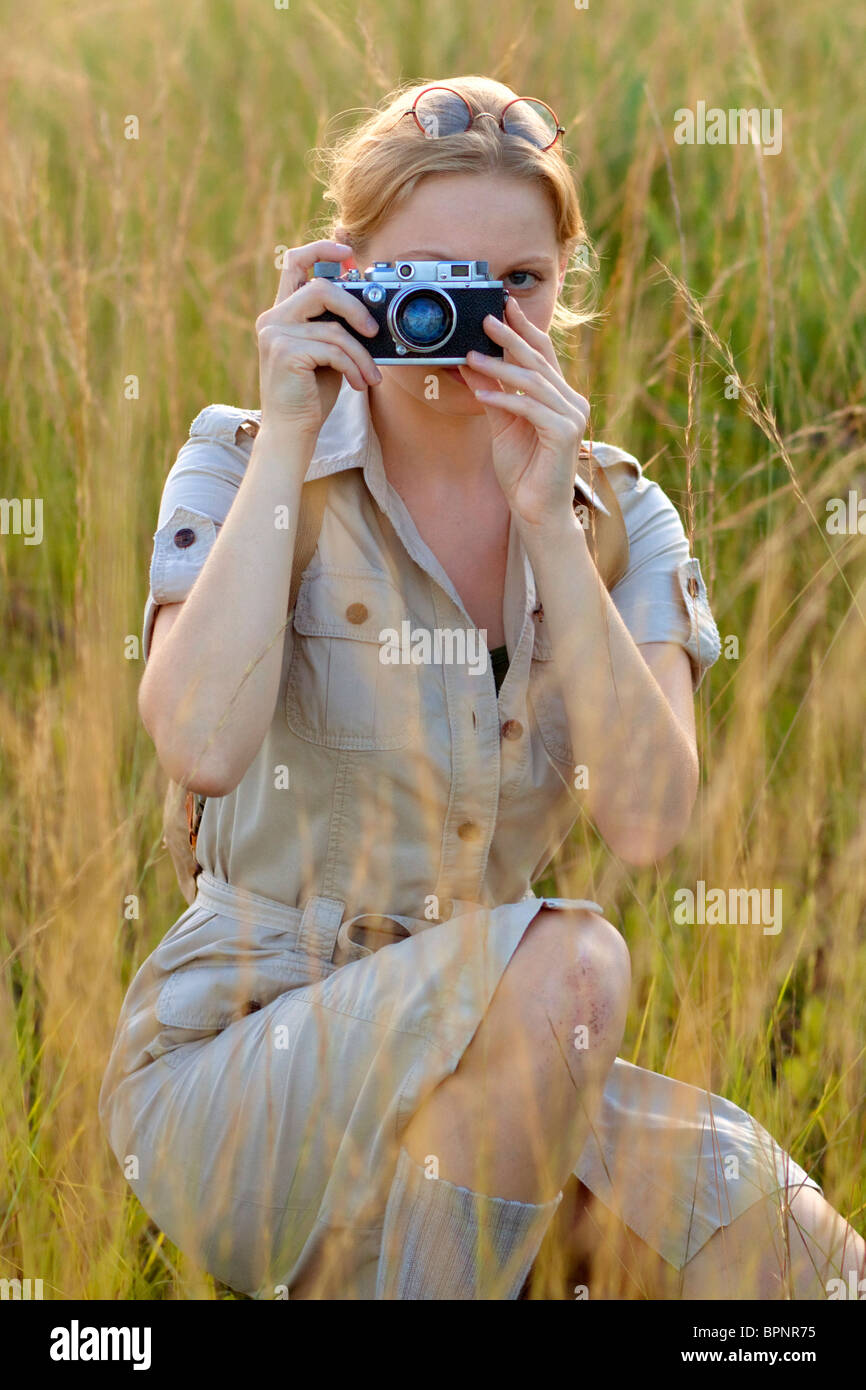 Young woman kneeling in field while taking a photograph Stock Photo - Alamy
