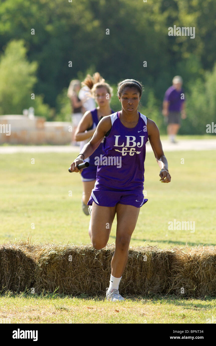 African-American female high school runner jumps hay bale on cross ...