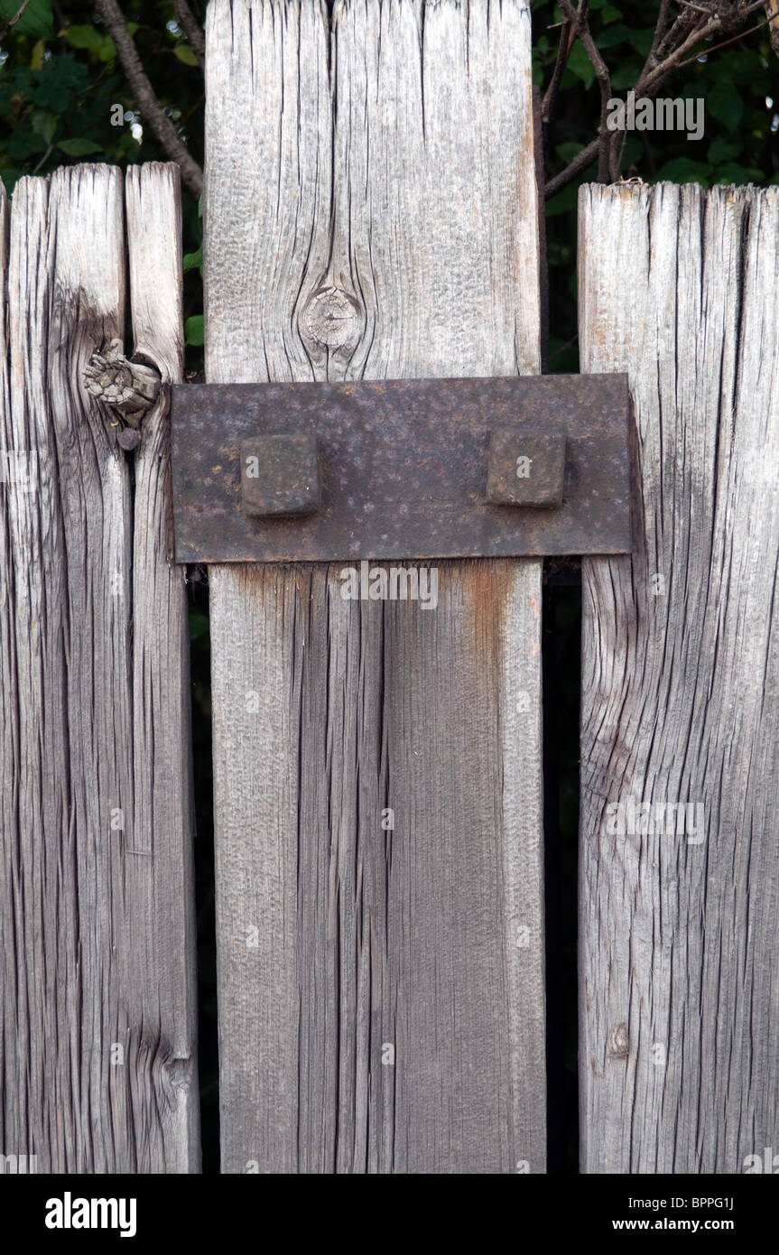 A rickety old wooden fence reinforced and repaired with a rusty metal ...