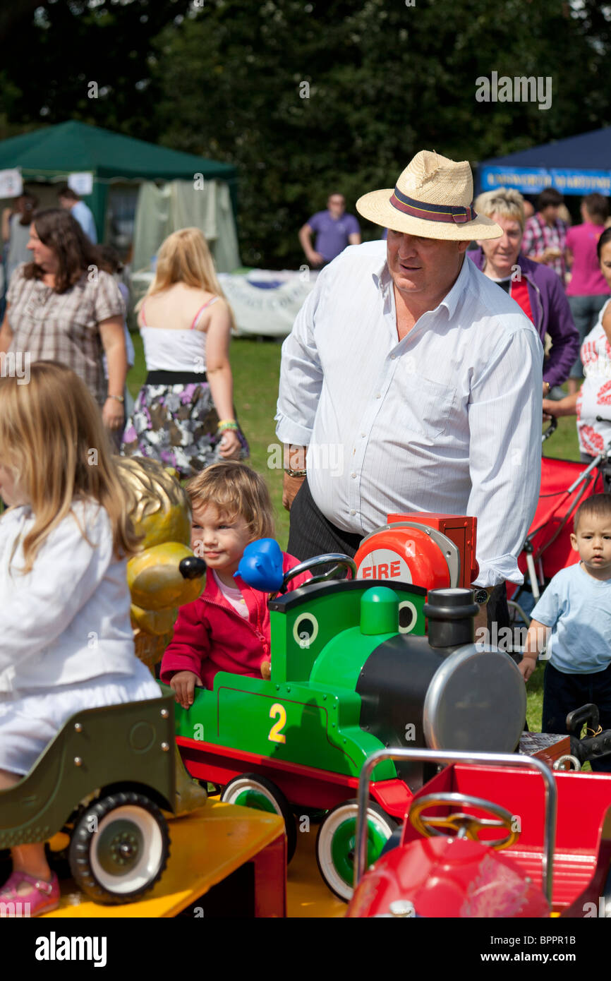 Man in hat operating hand powered fairground ride for toddlers Stock ...