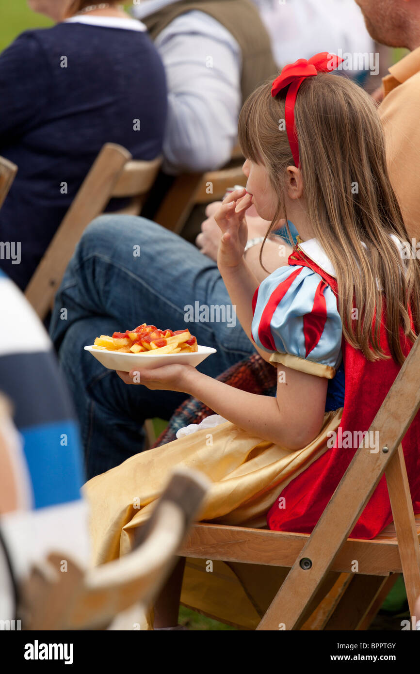 young girl in princess outfit eating chips with tomato ketchup seated ...