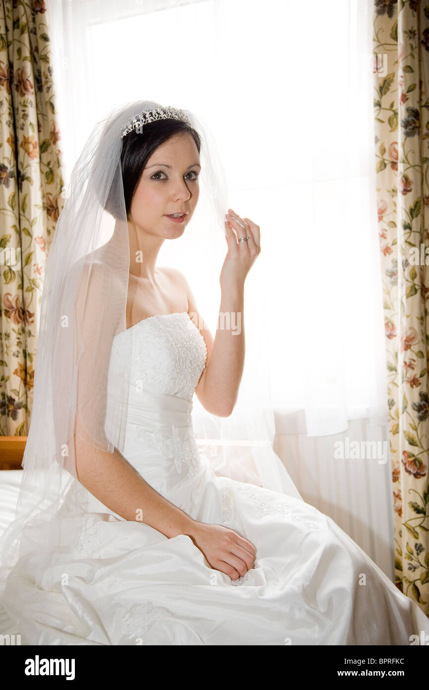 Beautiful young bride sitting on a bed Stock Photo - Alamy