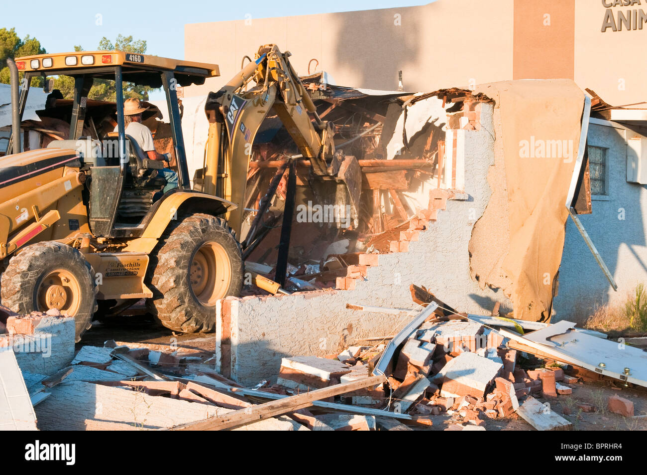 A backhoe is being used to knock down an old commercial building and ...