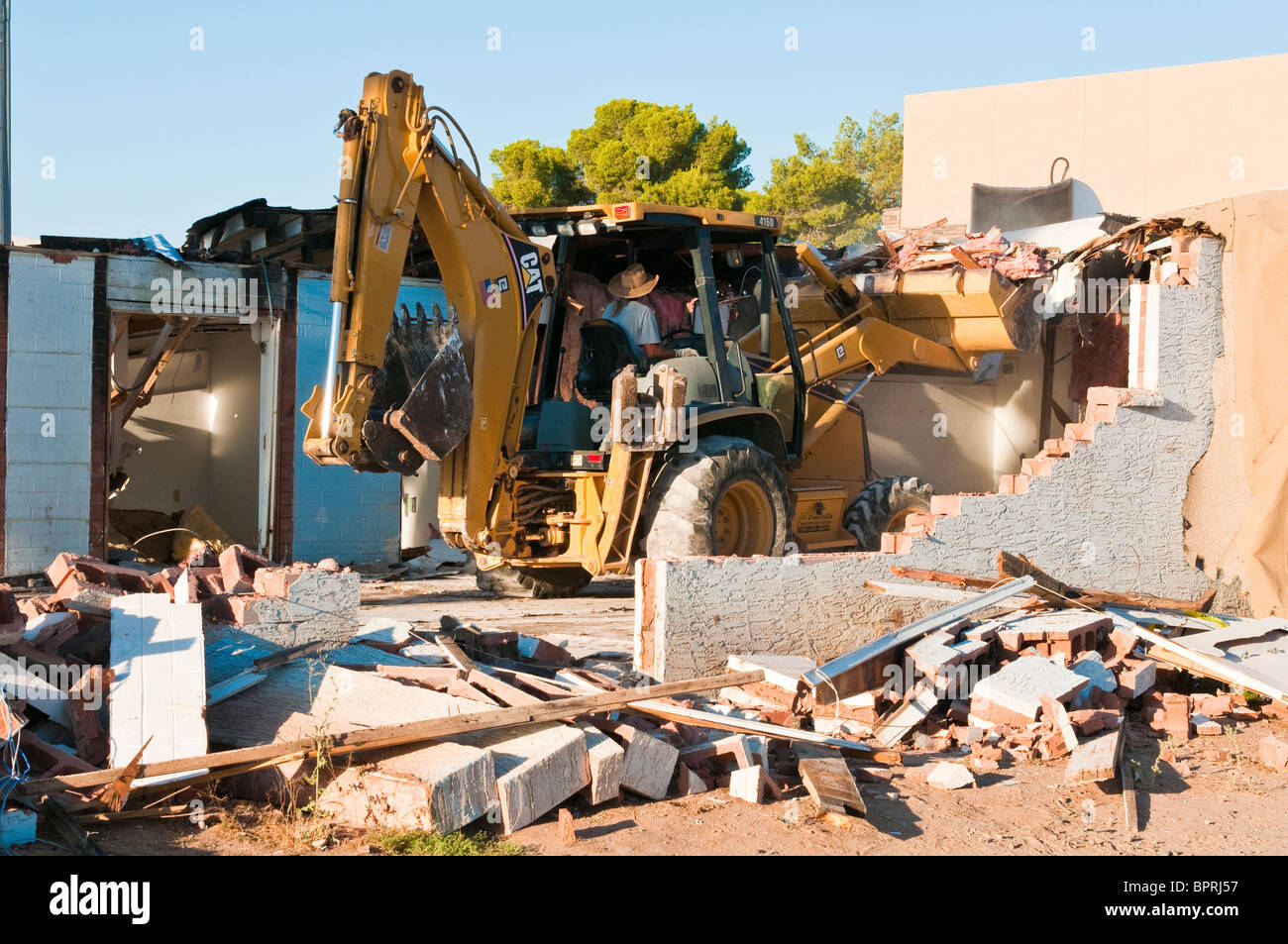 A backhoe is being used to knock down an old commercial building and ...