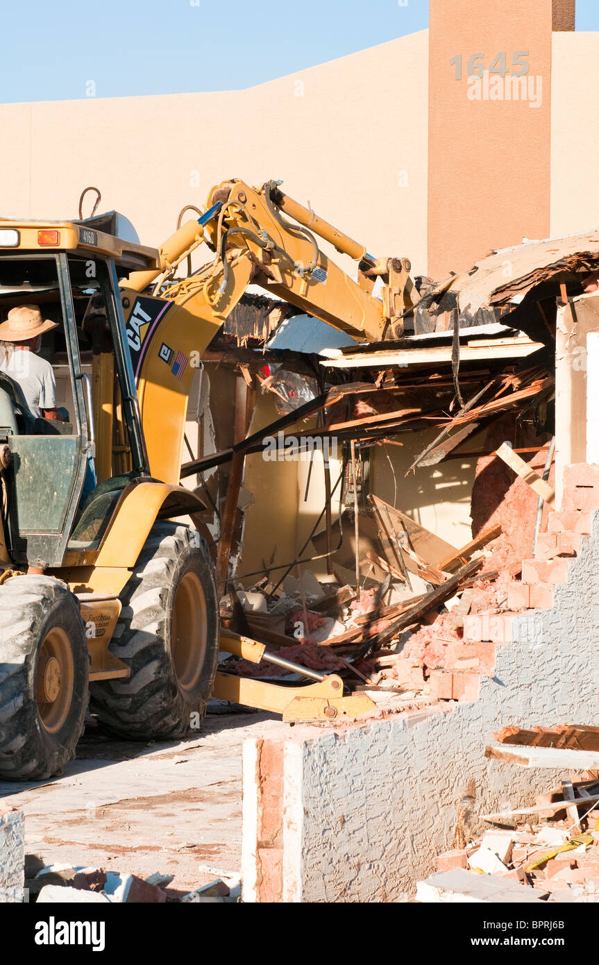 A backhoe is being used to knock down an old commercial building and ...
