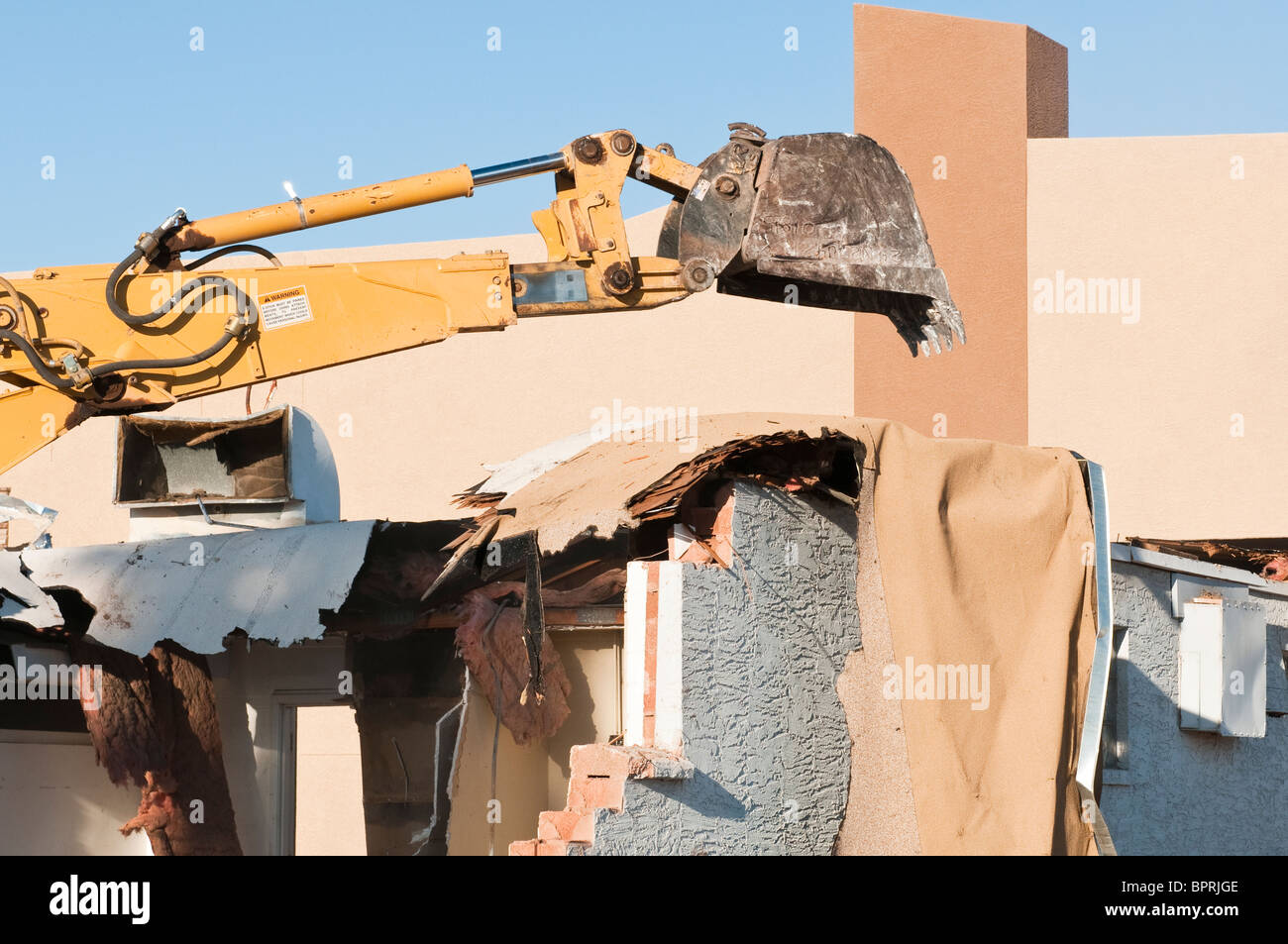 A backhoe is being used to knock down an old commercial building and ...
