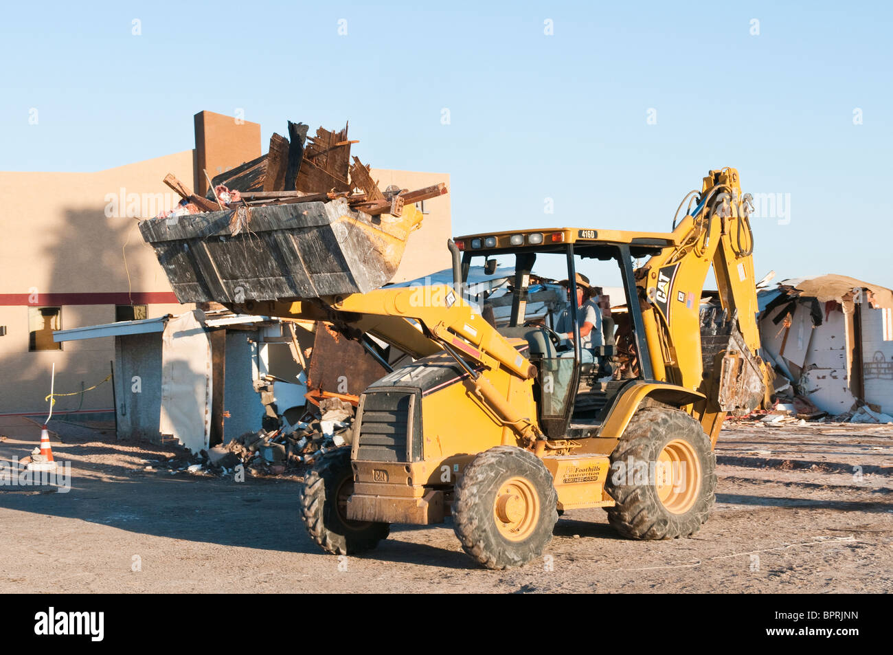 A backhoe is being used to remove debris from the demolition of an old ...