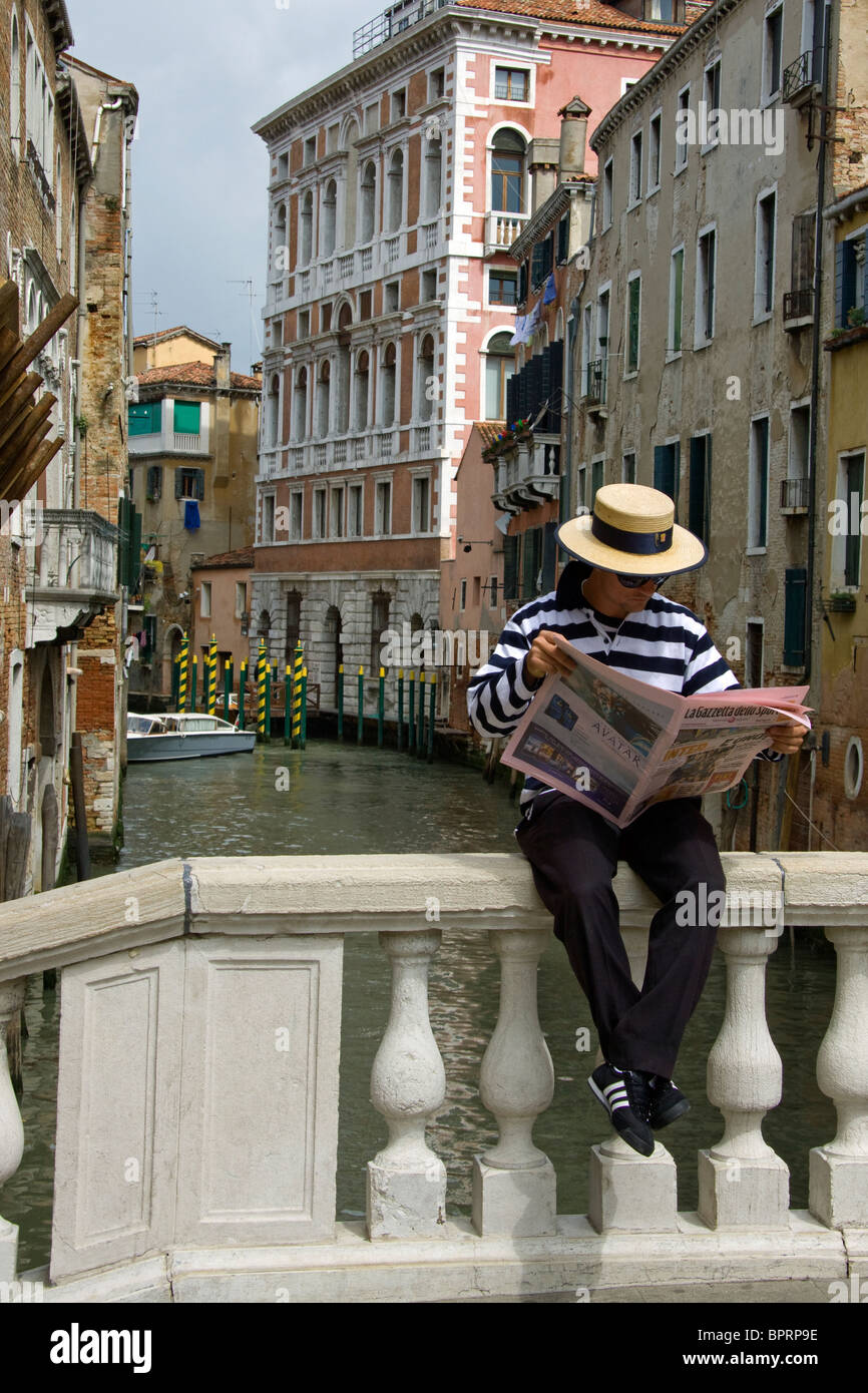 Gondolier reading newspaper on stone bridge in Venice Stock Photo - Alamy