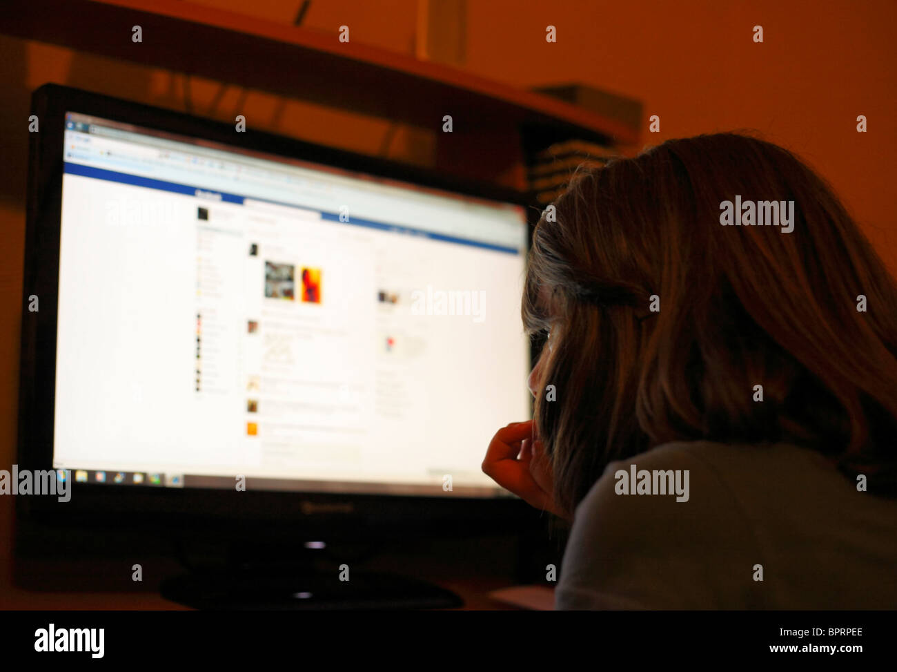 A young teenage girl looking into her Facebook page on a computer ...