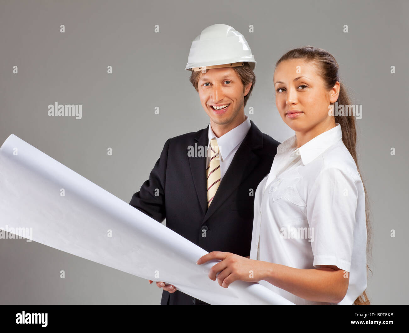 An architect wearing a hard hat and co-worker reviewing blueprints ...