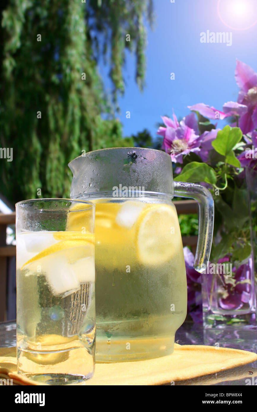 Lemonade in jar and glass with lemons, ice, on outdoor table with ...