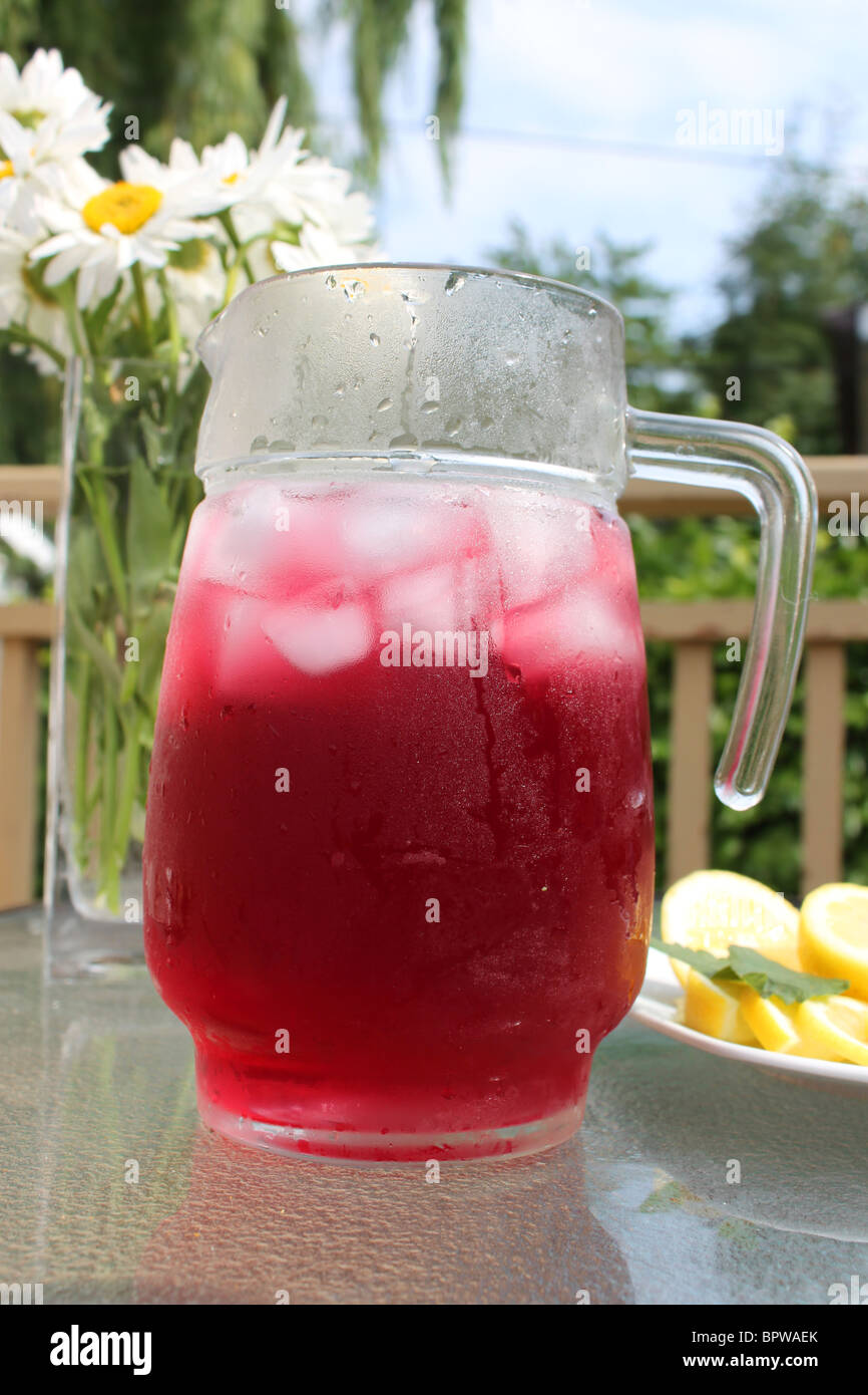 Jug with refreshing fruit punch with ice, flowers, lemons and greenery ...