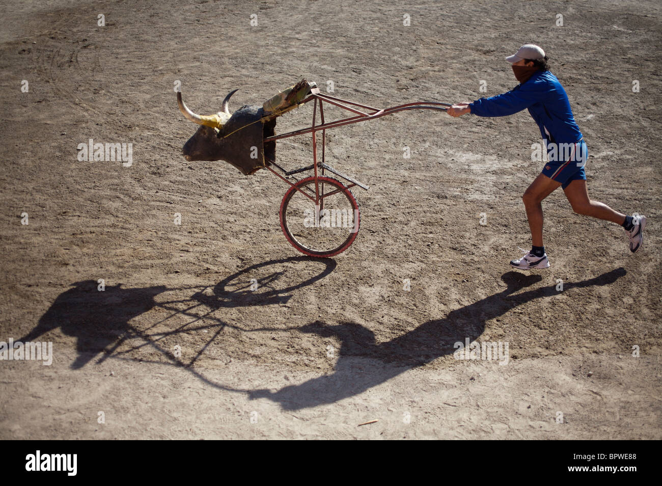 A bullfighter pushes a stuffed bull's head mounted on a bicycle wheel ...