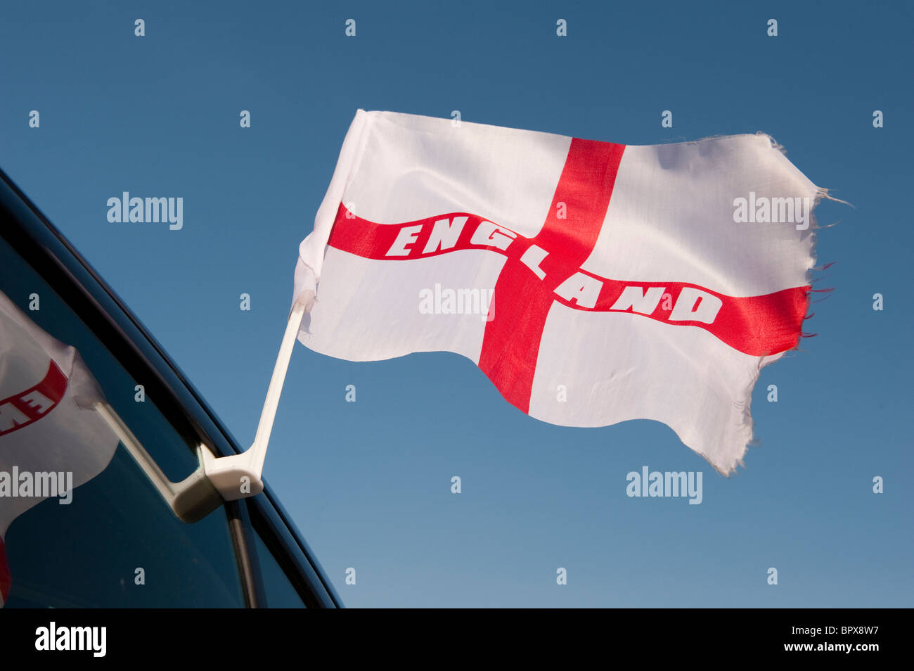 England flag fixed to a car window flying in a bright blue sky ...