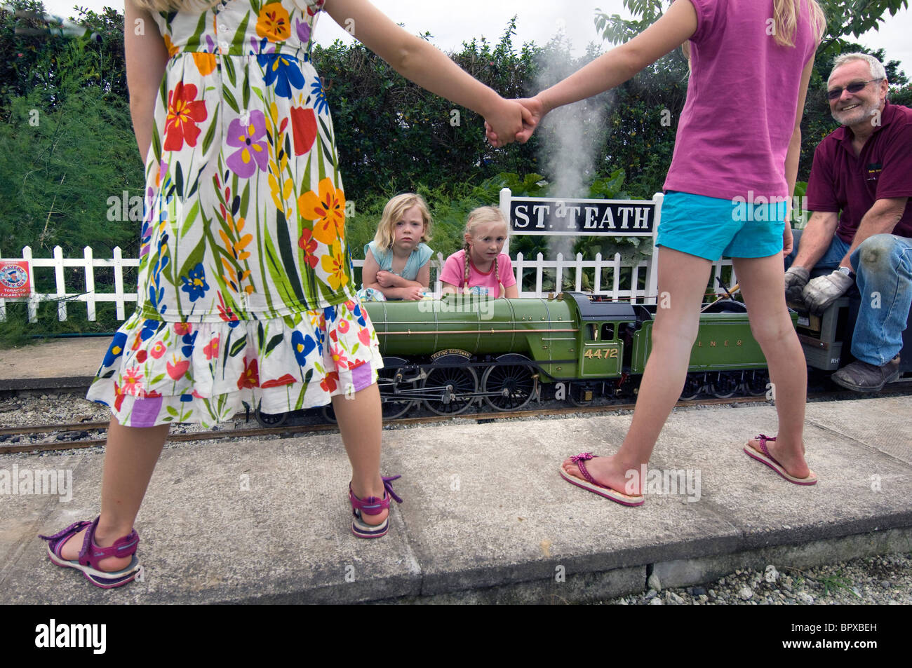 Children holding hands on the platform of a model railway as a little ...