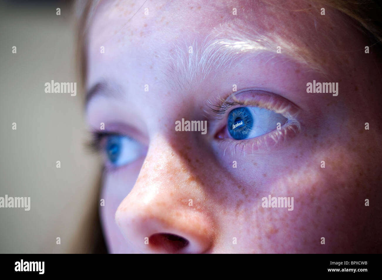 Young girl looking at computer screen with facebook logo reflected in ...
